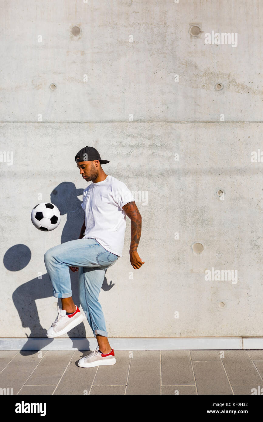Young man playing with soccer ball in front of concrete wall Stock ...