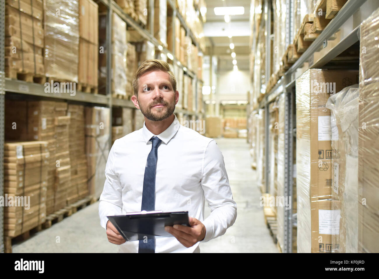 Businessman with clipboard in warehouse looking at shelves Stock Photo ...