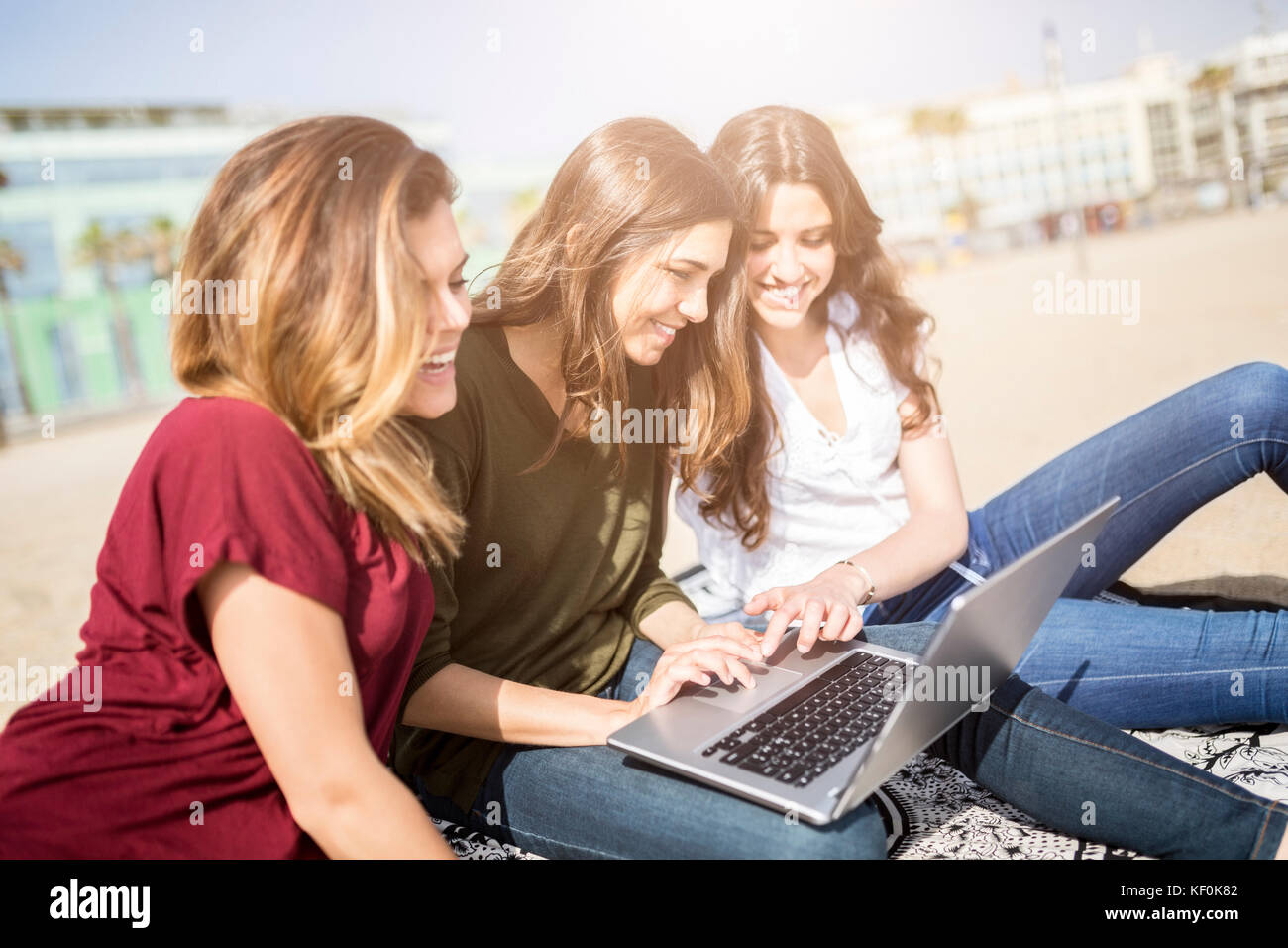 Three happy female friends using a laptop on the beach Stock Photo - Alamy