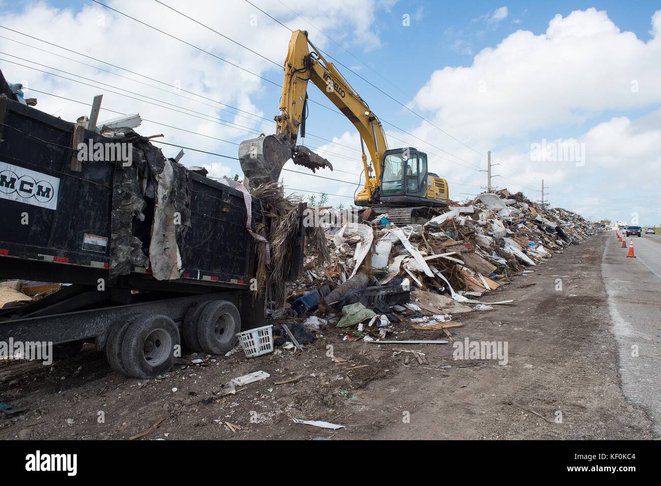 An excavator removes trash and debris on the side of Overseas Highway ...