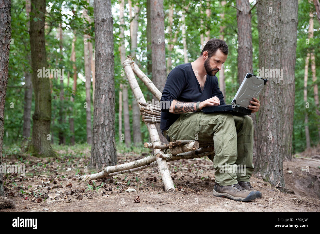 Man sitting on self-made wooden chair in forest using laptop Stock ...