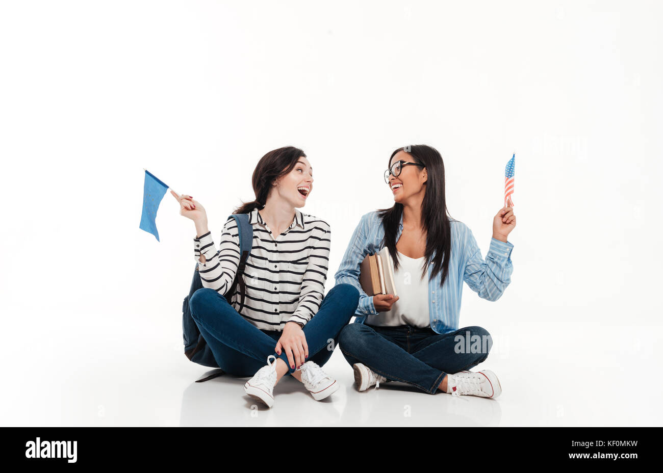 Two happy joyful female students waving us flags while sitting together ...