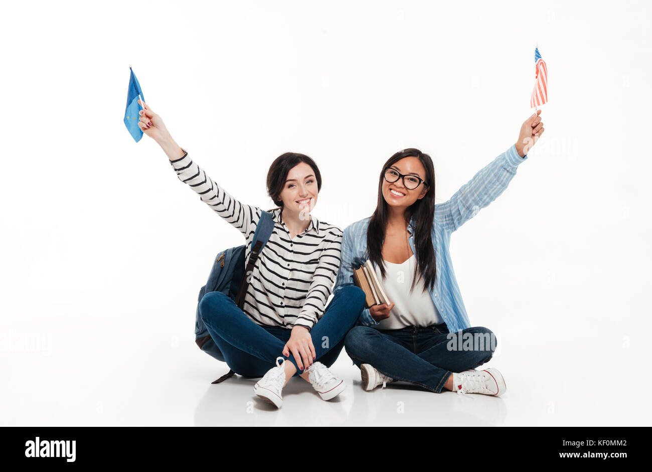 Two joyful female students waving us flags while sitting together on ...