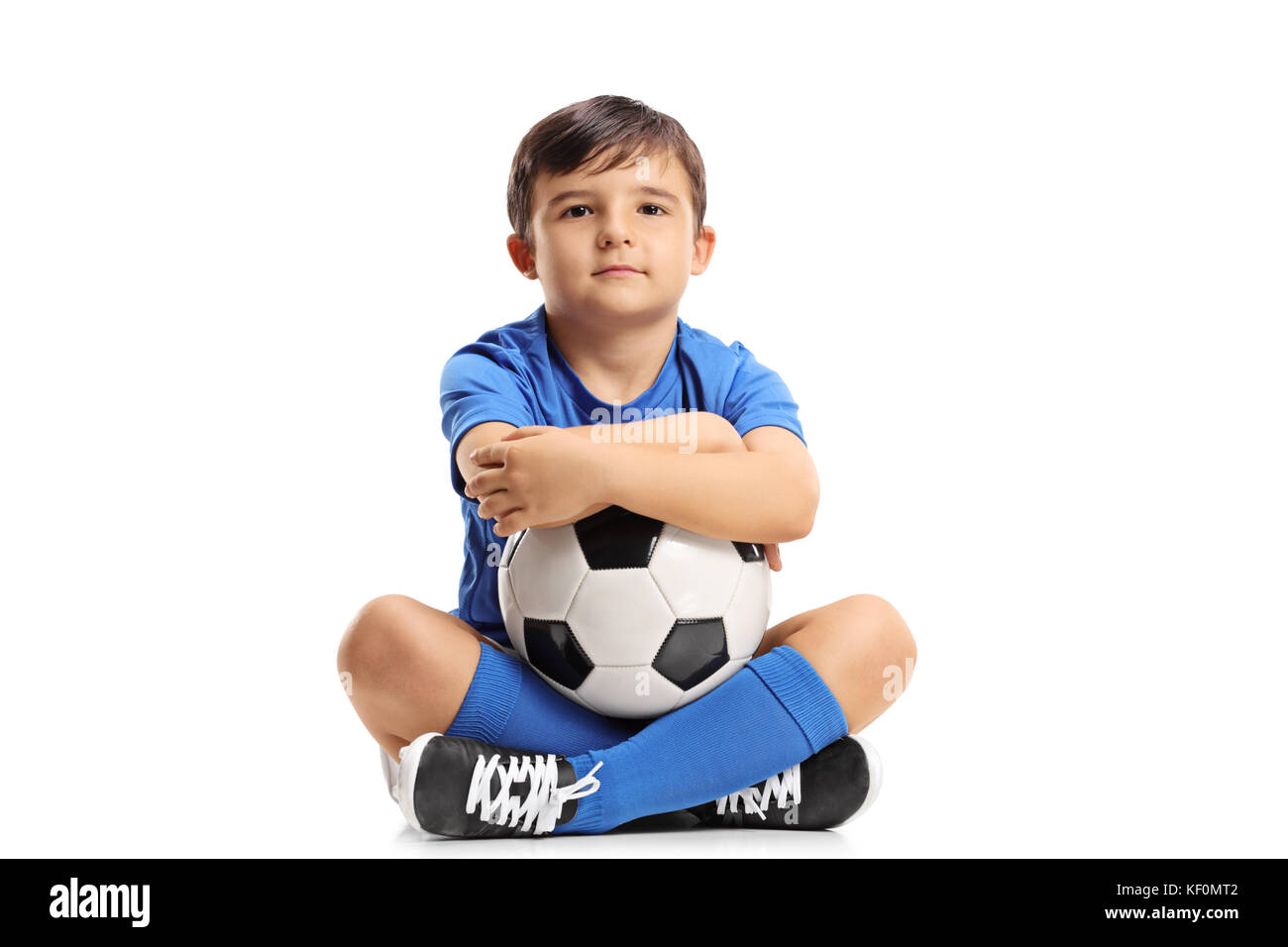 Little footballer sitting on the floor and looking at the camera ...