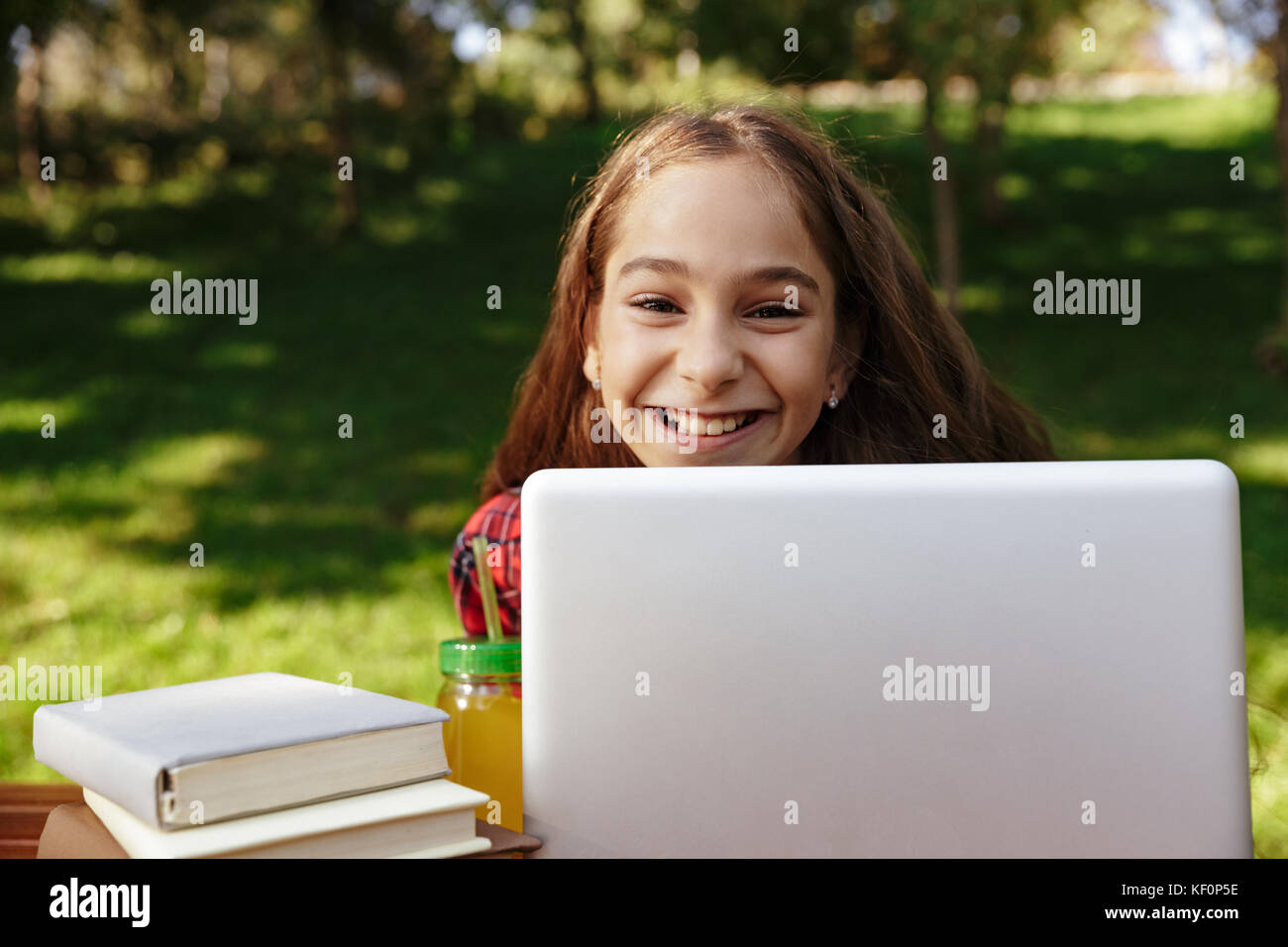 Happy young brunette girl sitting by the table with laptop computer and ...