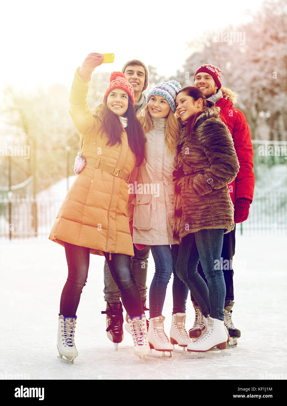 happy friends with smartphone on ice skating rink Stock Photo - Alamy