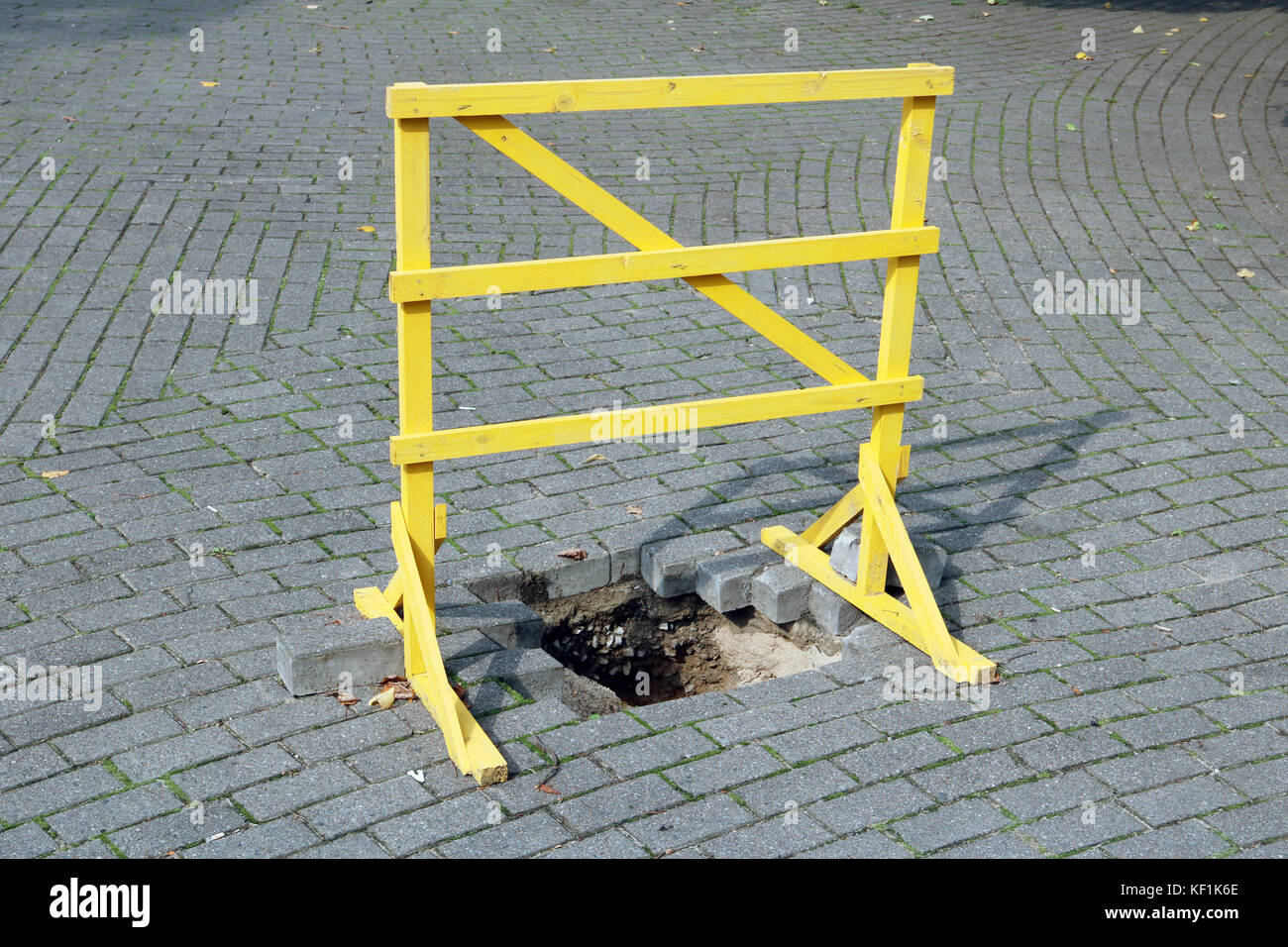 A homemade wooden yellow barrier stands over a pit in an urban granite ...