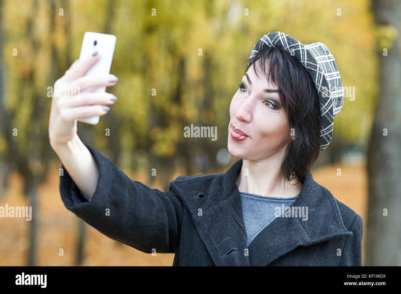 girl taking selfie in autumn city park, make faces, yellow leaves and ...