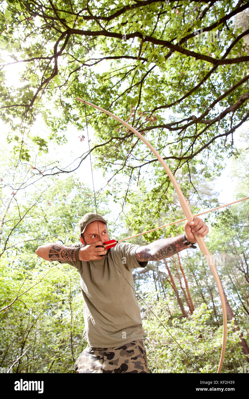 Man shooting with bow and arrow in the forest Stock Photo - Alamy