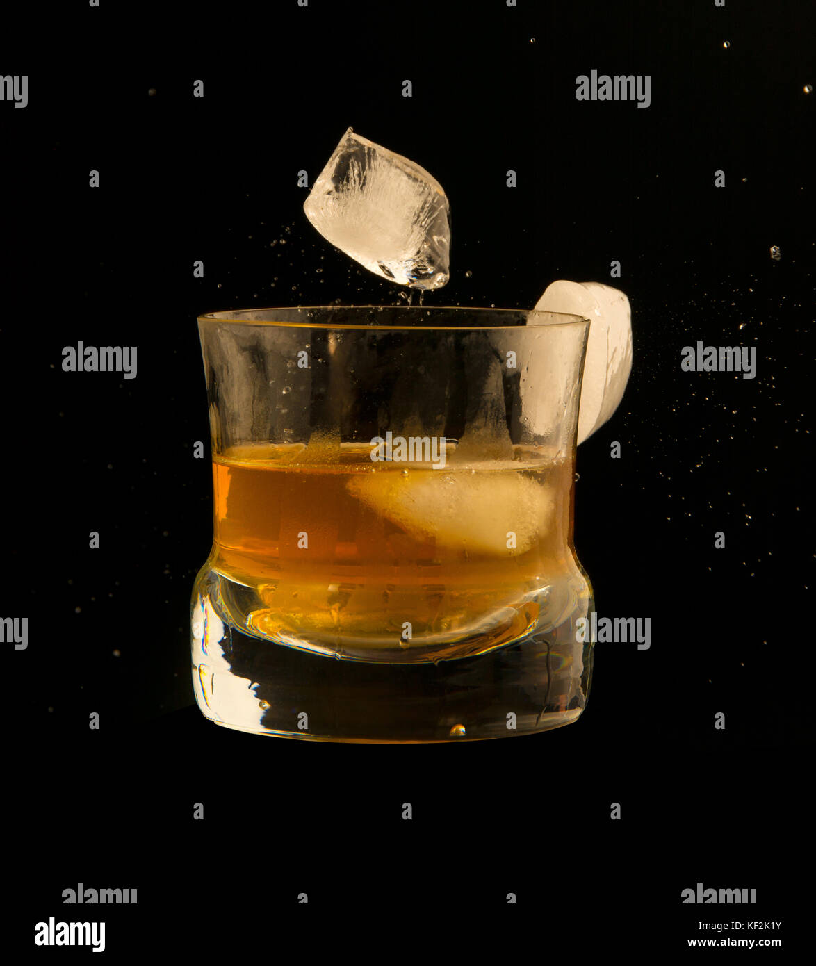 ice falling on a glass of whiskey making a splash, liquid floating ...
