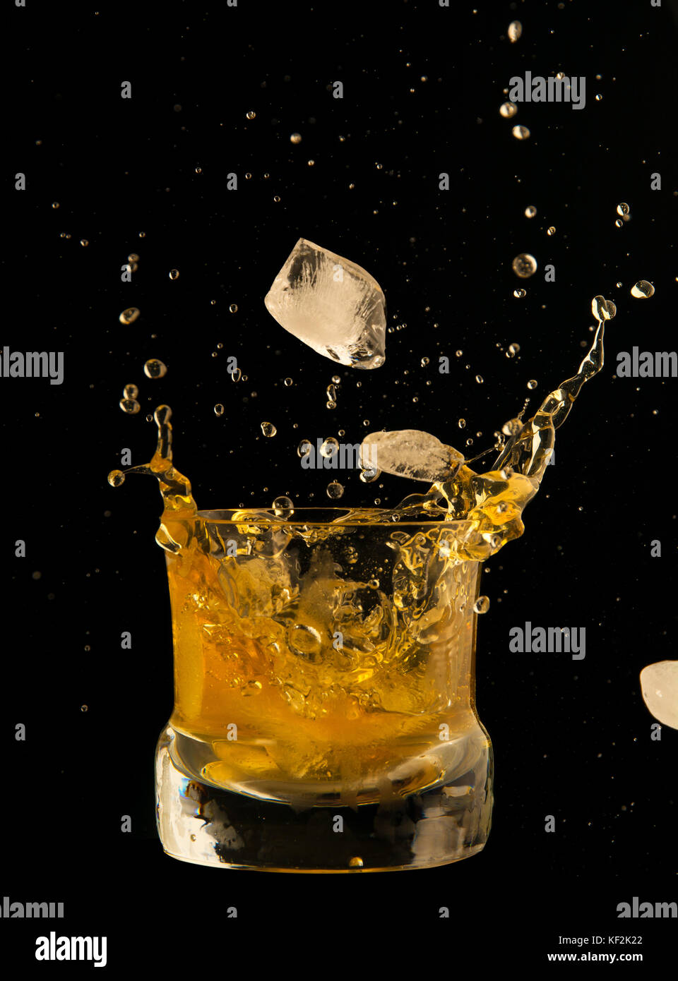 ice falling on a glass of whiskey making a splash, liquid floating ...