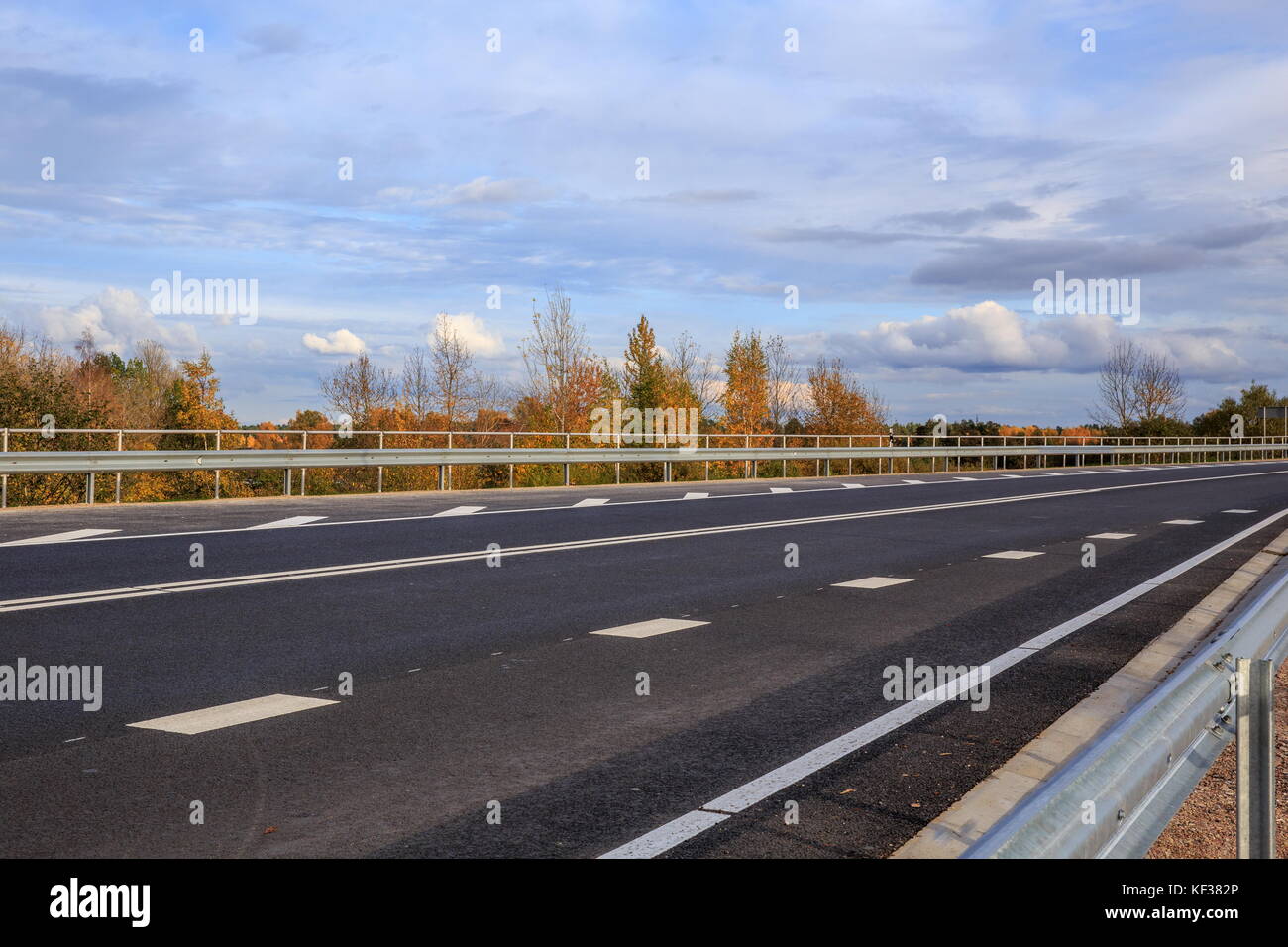 Road up hill and autumn fall landscape under white clouds and blue sky ...