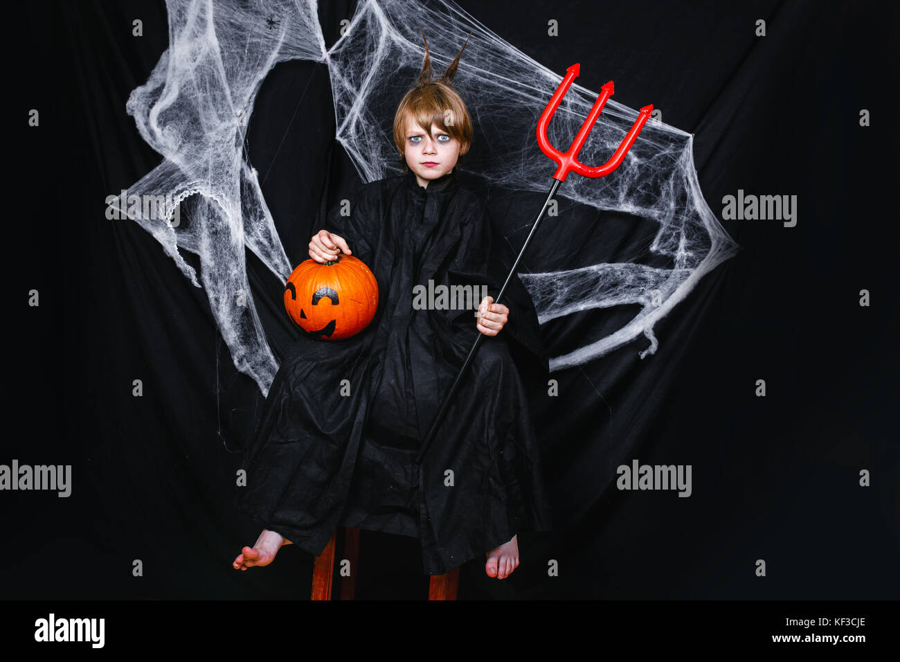 Cute little boy sitting on the pumpkin on black background with a ...
