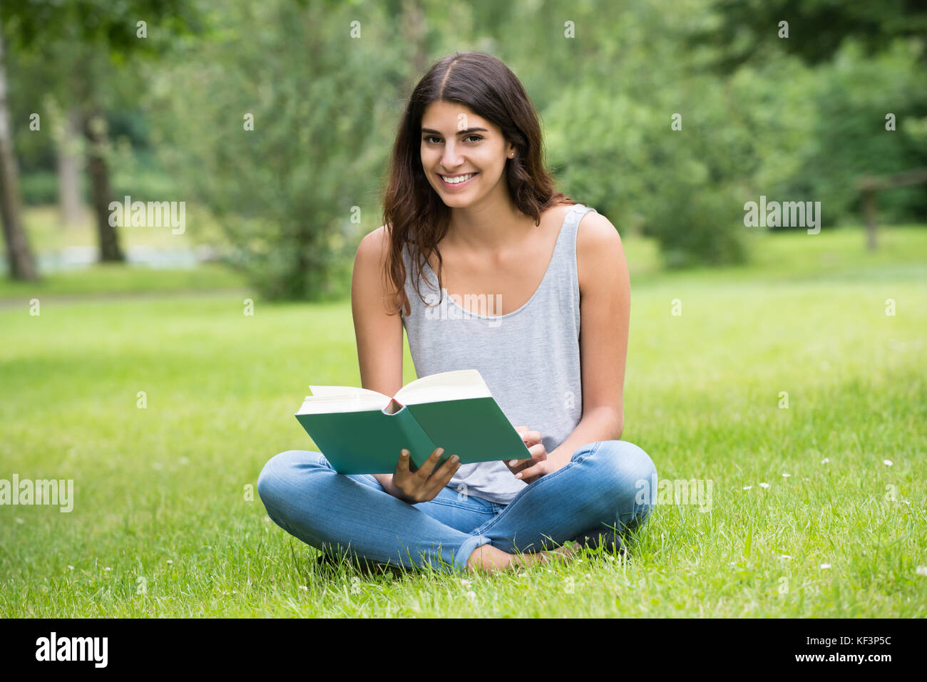 Smiling Young Woman Sitting On Green Grass Reading Book In Park Stock ...