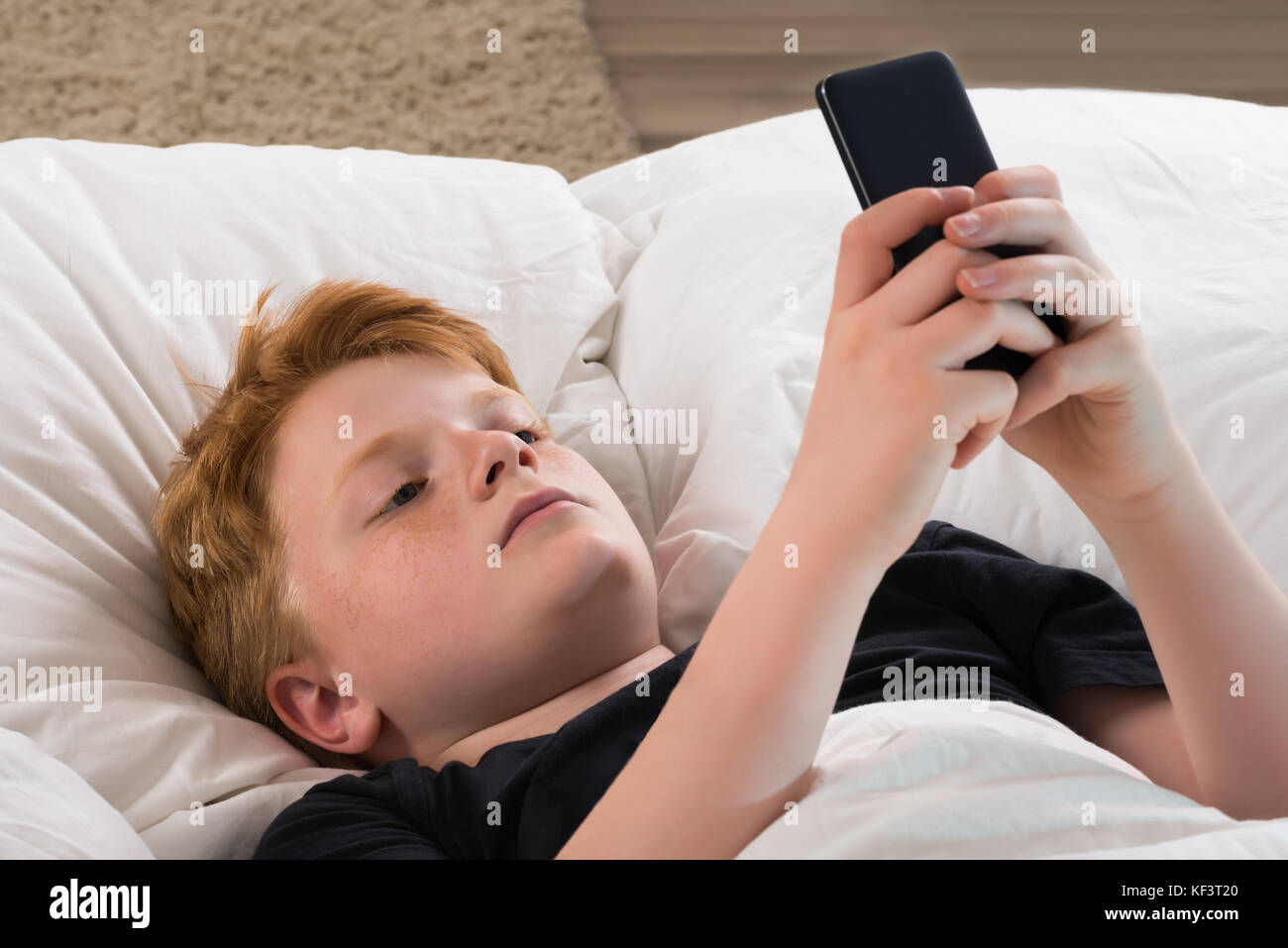 Boy Lying On Bed Holding Mobile Phone Stock Photo - Alamy