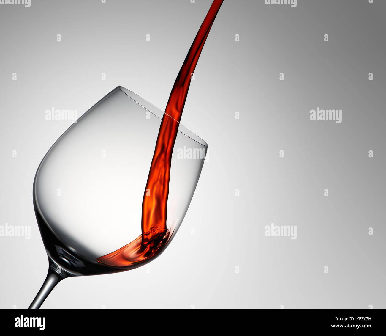 Red wine poured into elegant wine glass on grey gradient Stock Photo ...