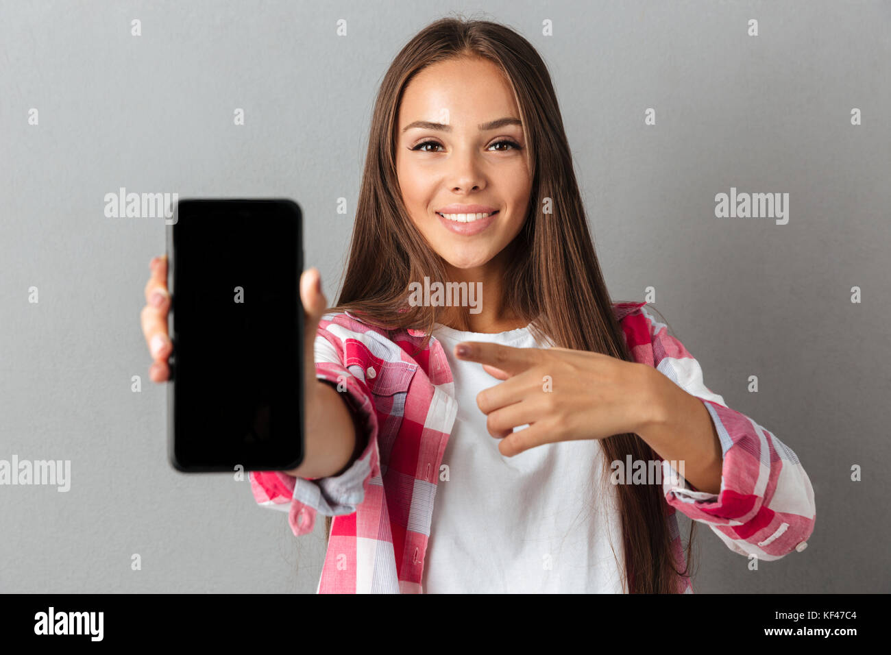 Young pretty smiling woman pointing with finger on phone screen, over ...