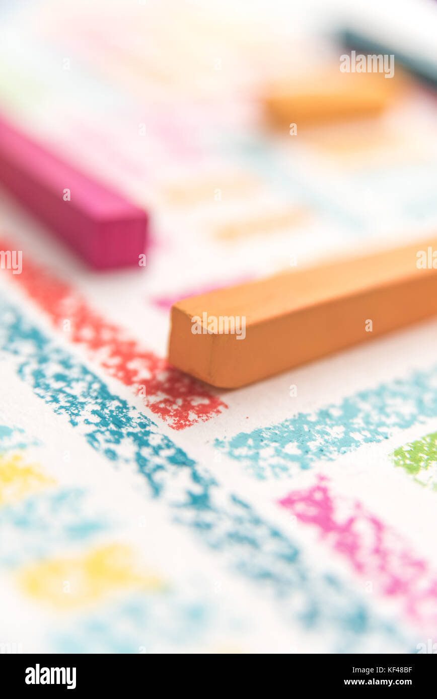 Cropped photo of pieces of chalk, over abstract colorful background ...