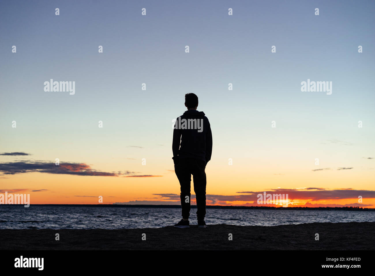 A young guy on the beach looking at the sunset Stock Photo - Alamy