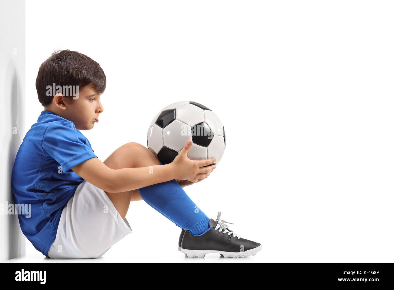 Disappointed little footballer leaning against a wall isolated on white ...