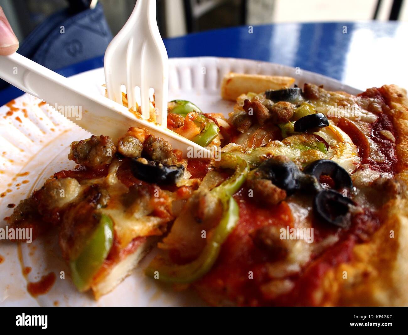 Photo of a pizza on a plate being sliced by plastic fork and knife ...