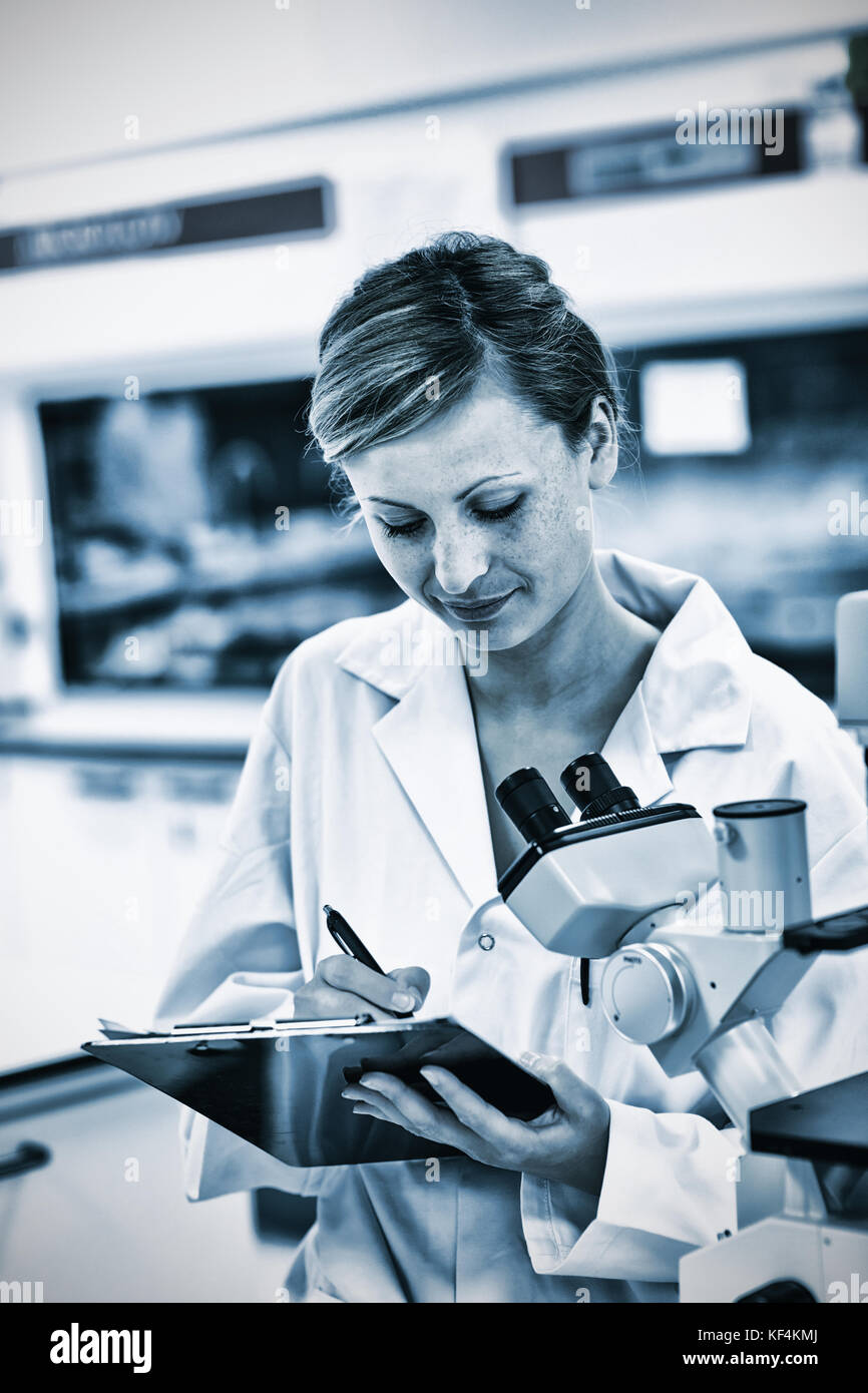 Serious female scientist writing on her clipboard in front of a ...