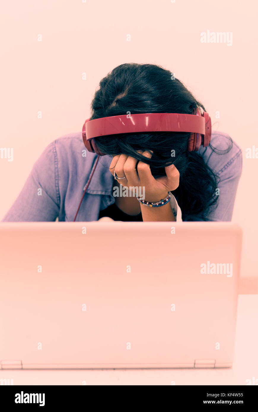 Young woman facing down seated in front of a laptop and supporting her ...