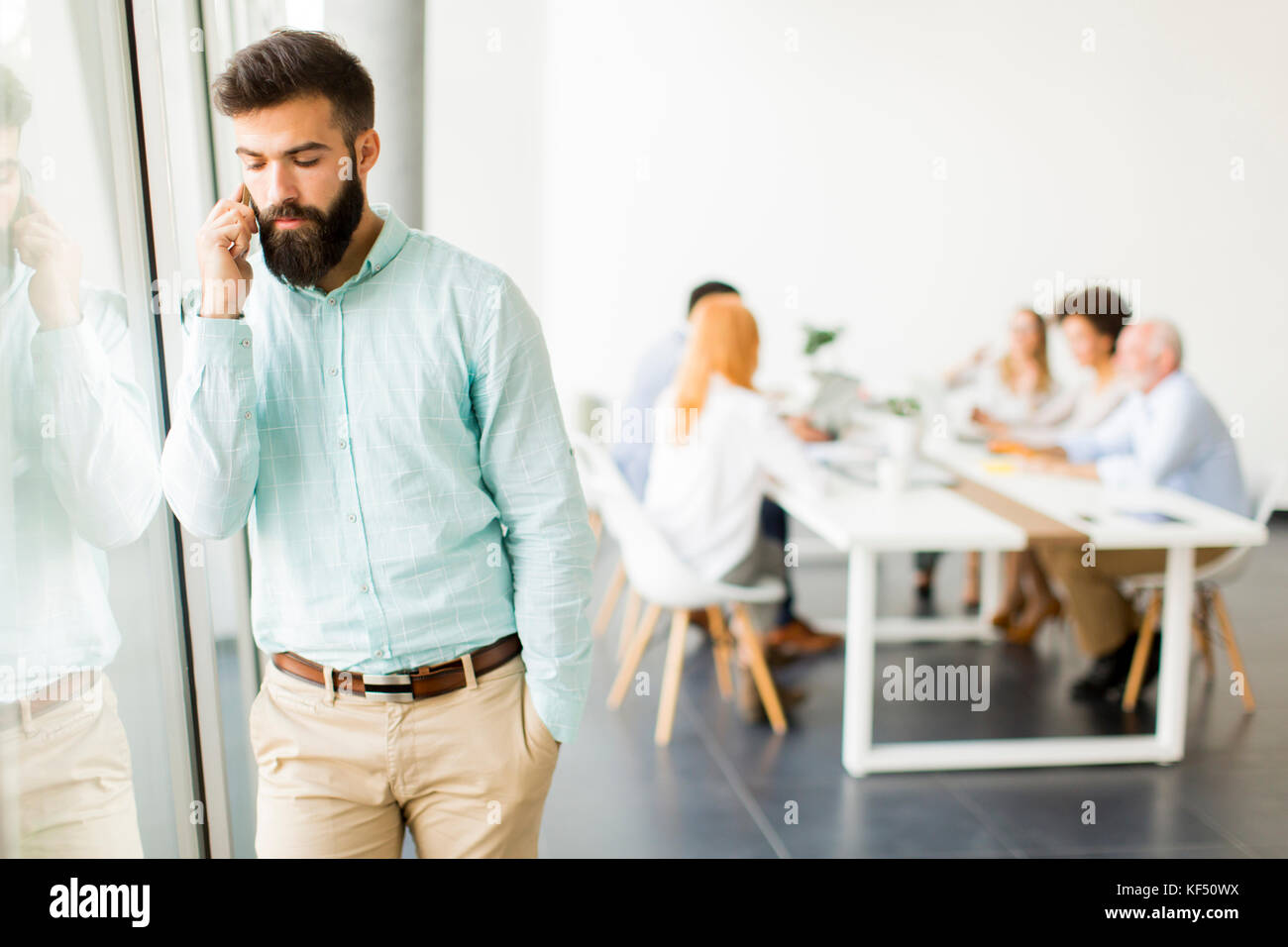 Young businessman using mobile phone in office while other people in ...