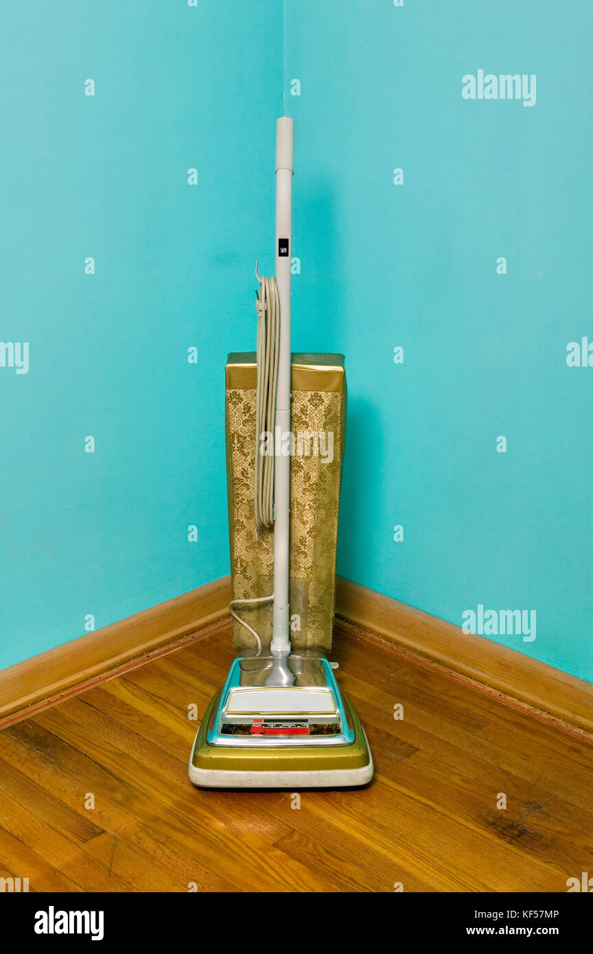 Vintage vacuum cleaner standing in room corner against turquoise walls ...