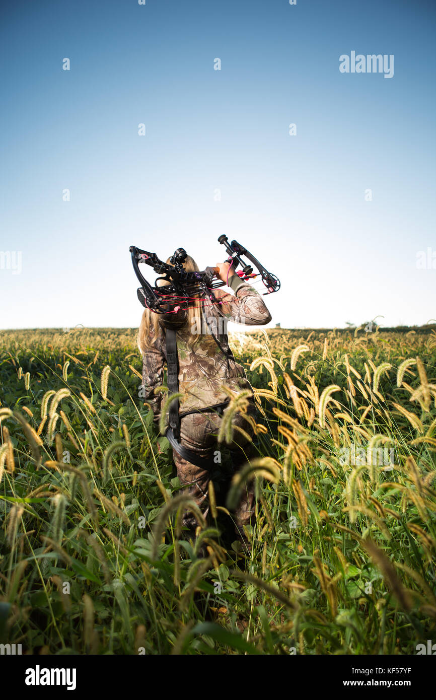 Hunter with bow wearing camouflage walking through tall grass in meadow ...