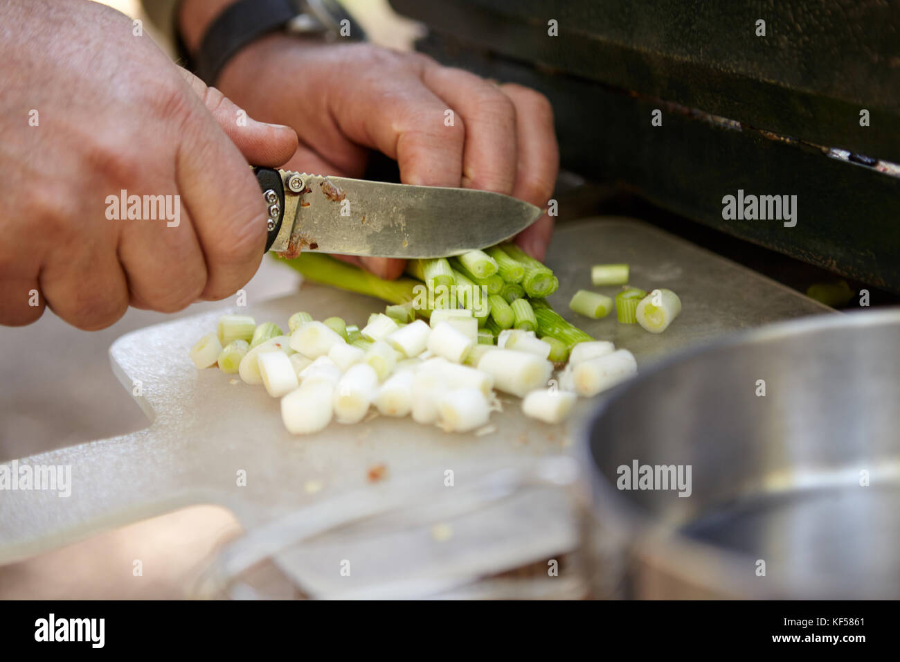 Close up view of person cutting spring onion with knife in kitchen ...