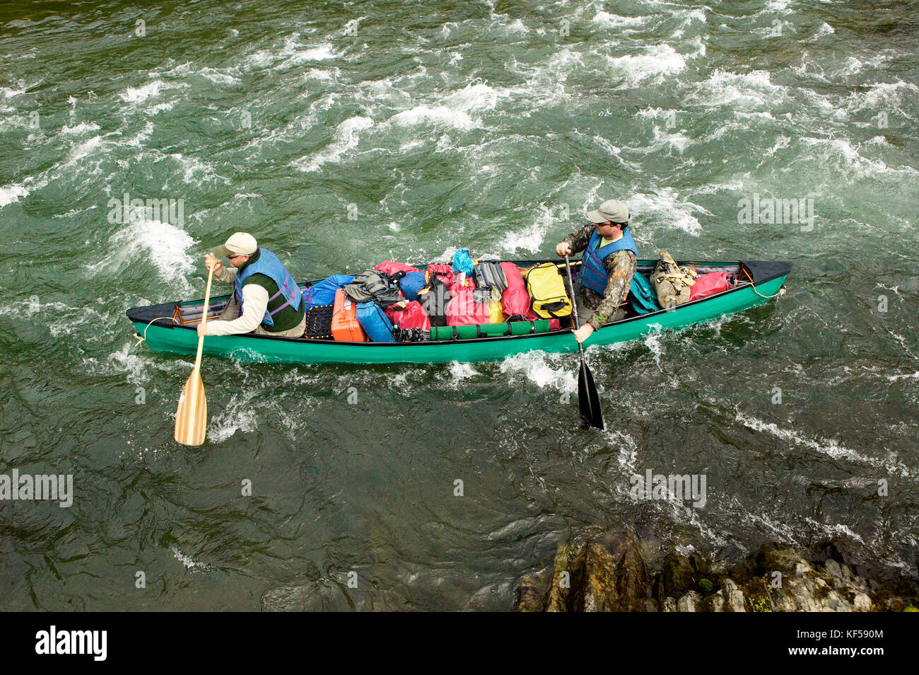 Two men navigate an overloaded canoe through rushing rapids during an ...
