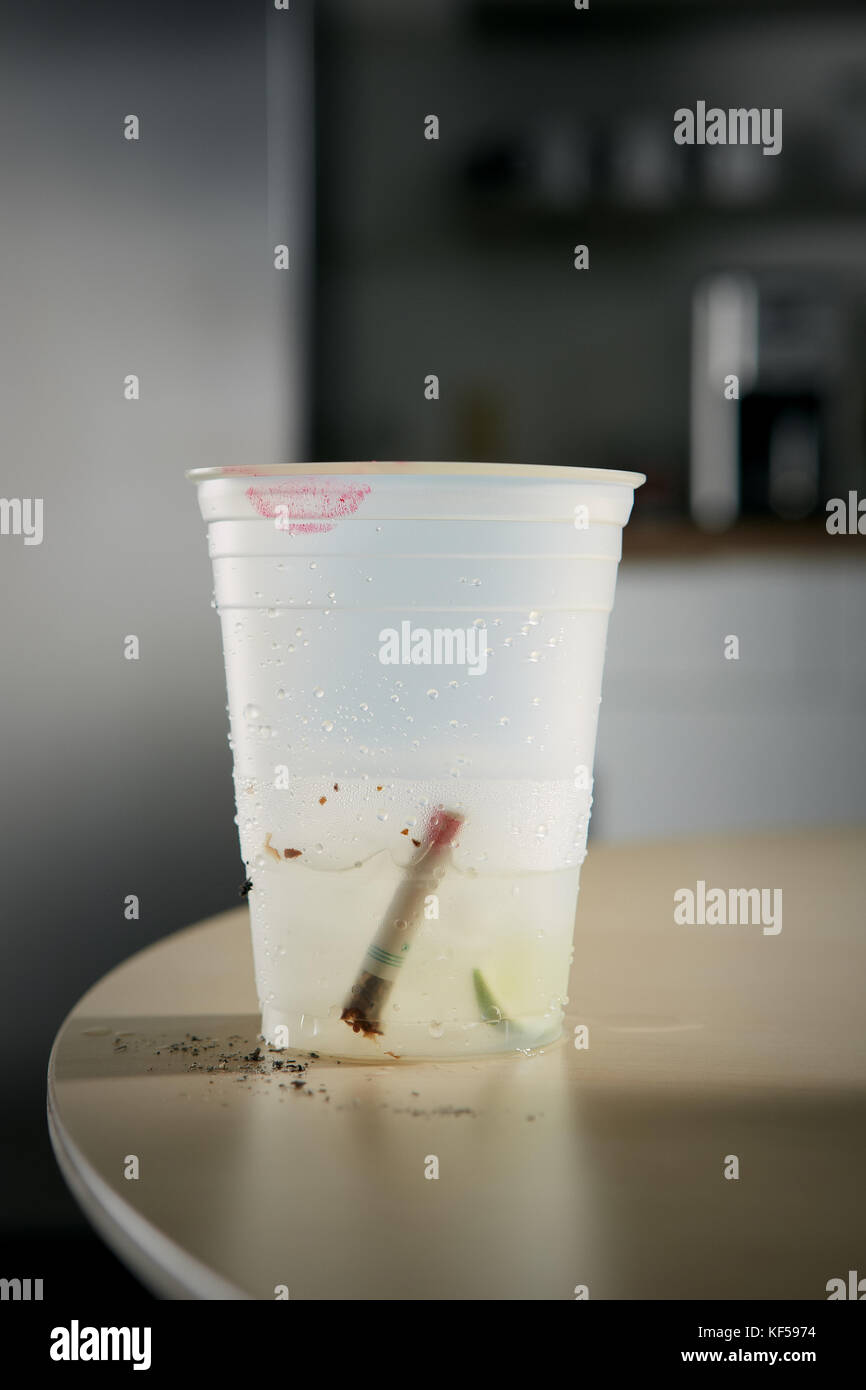 Cigarette extinguished in disposable plastic glass with red lip print ...
