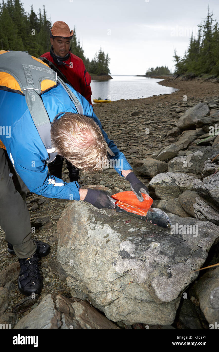Man cutting fish with knife on large stone by river Stock Photo - Alamy