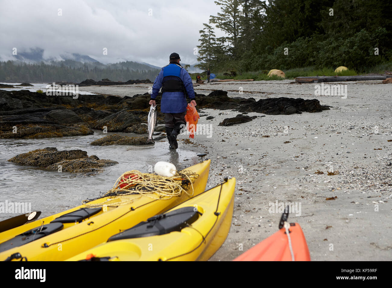 Fisherman carrying his catch along a beach away from the camera with ...