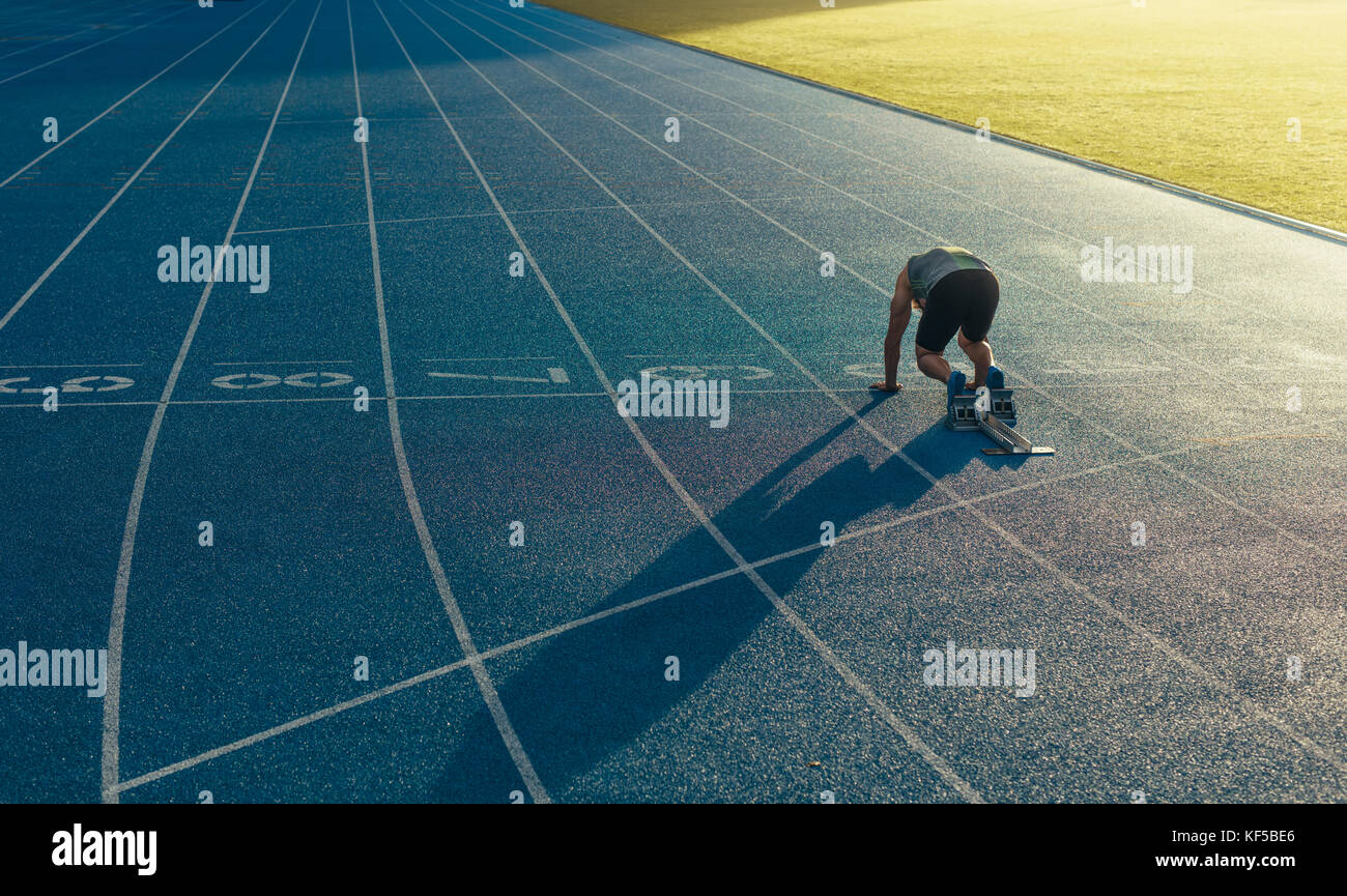 Rear view of an athlete ready to sprint on an all-weather running track ...