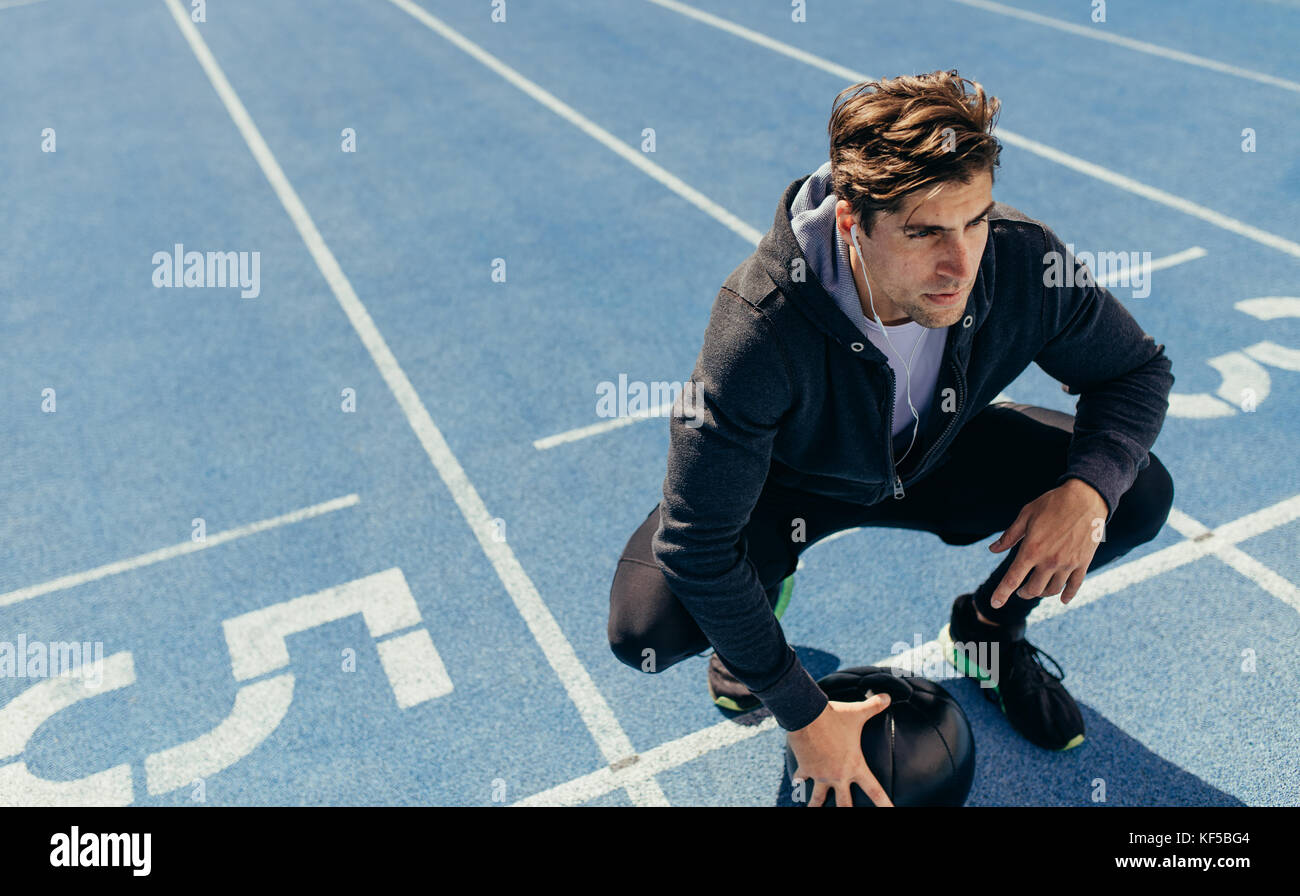 Athlete sitting on a running track near the start line with a medicine ...