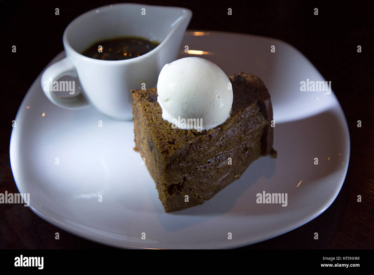 Sticky toffee pudding served with vanilla ice cream. A jug of sauce ...