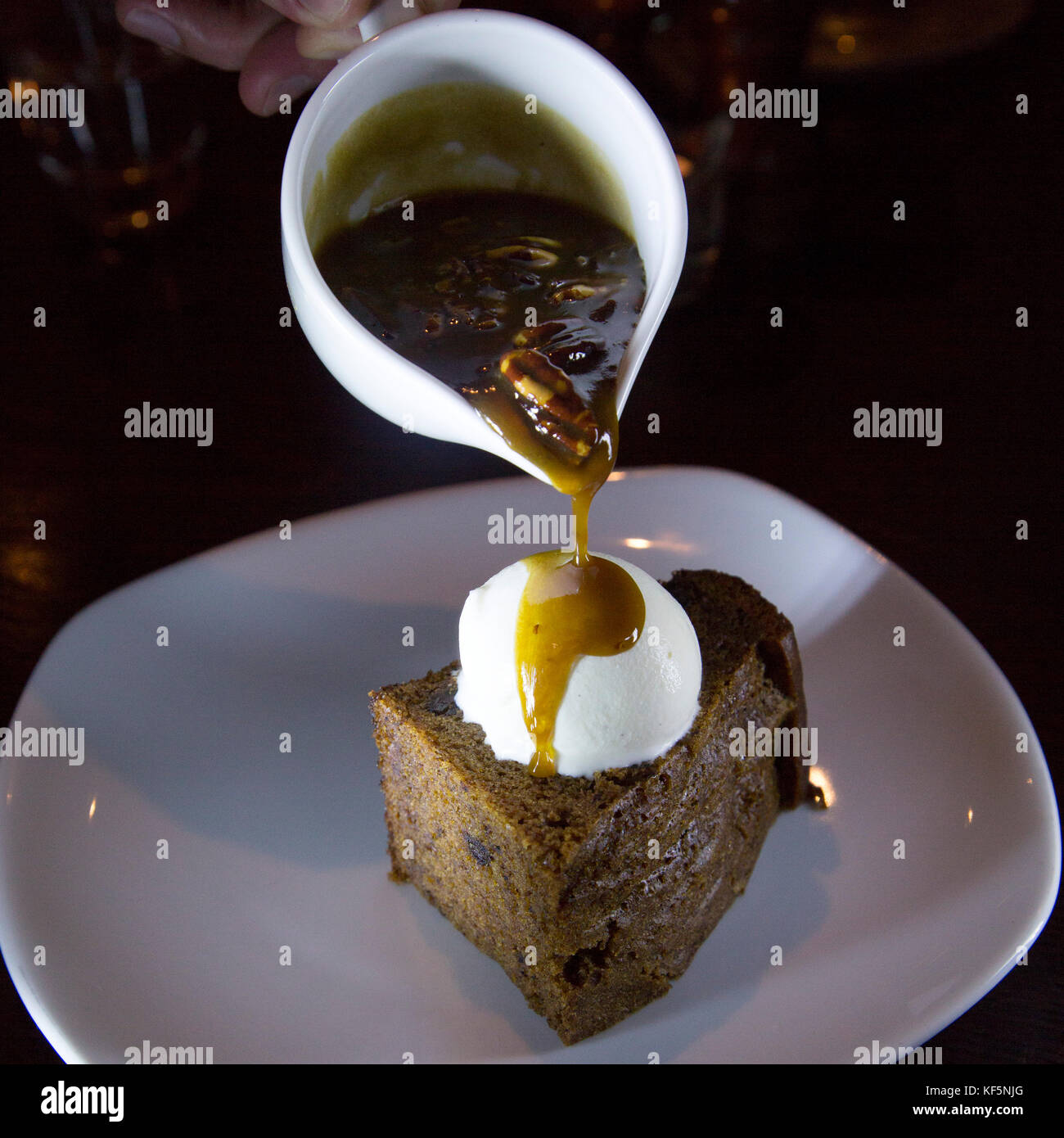 Sticky toffee pudding served with vanilla ice cream. A jug of sauce ...