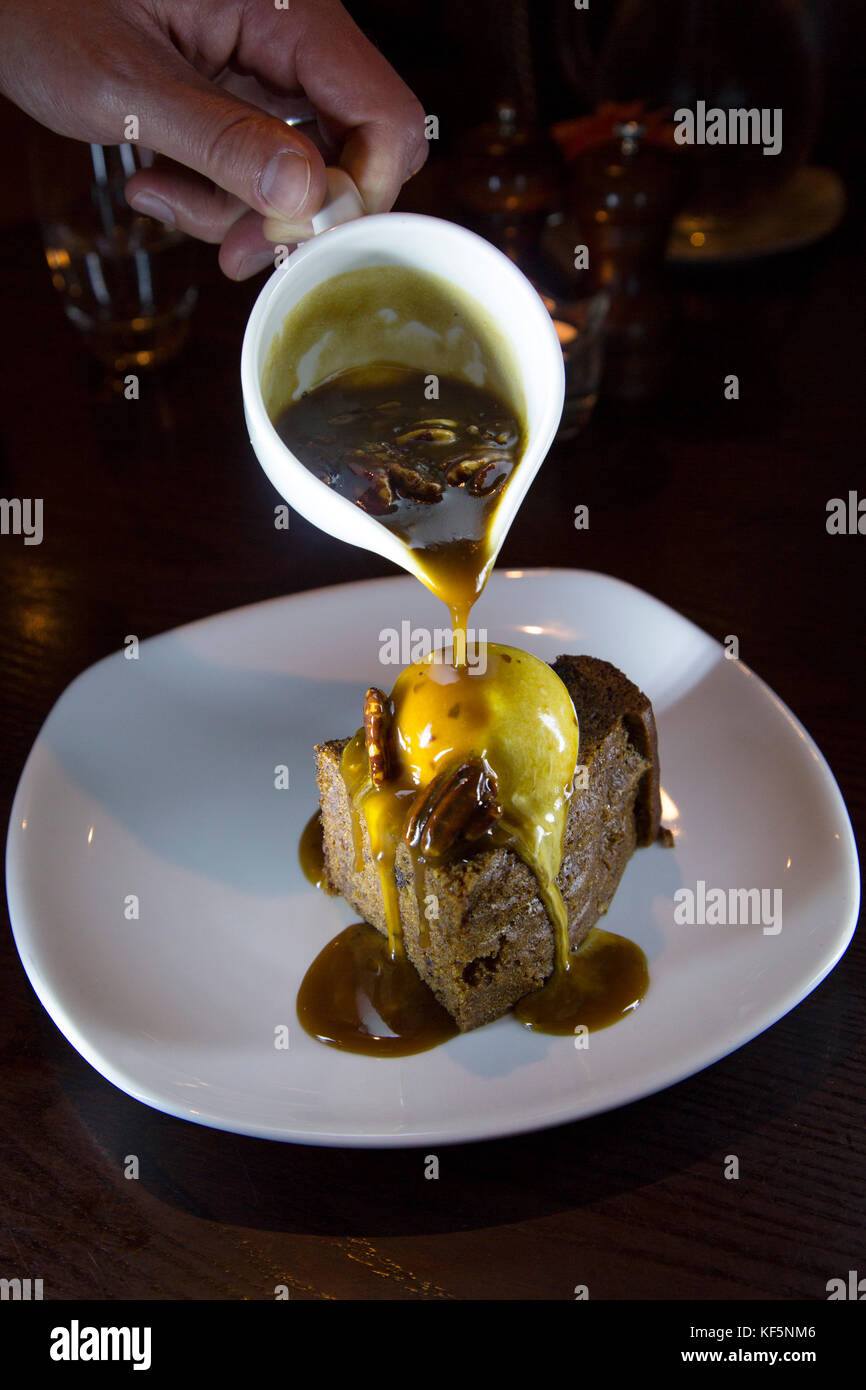 Sticky toffee pudding served with vanilla ice cream. A jug of sauce ...