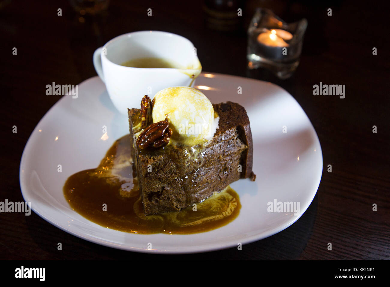 Sticky toffee pudding served with vanilla ice cream. A jug of sauce ...