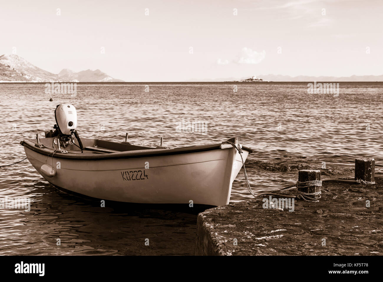 A sepia/split toned image of a small fishing boat moored to the waters ...