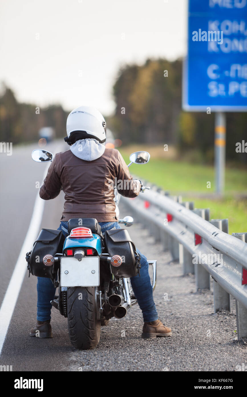 Rear view at female motorcycle driver resting on roadside on country ...