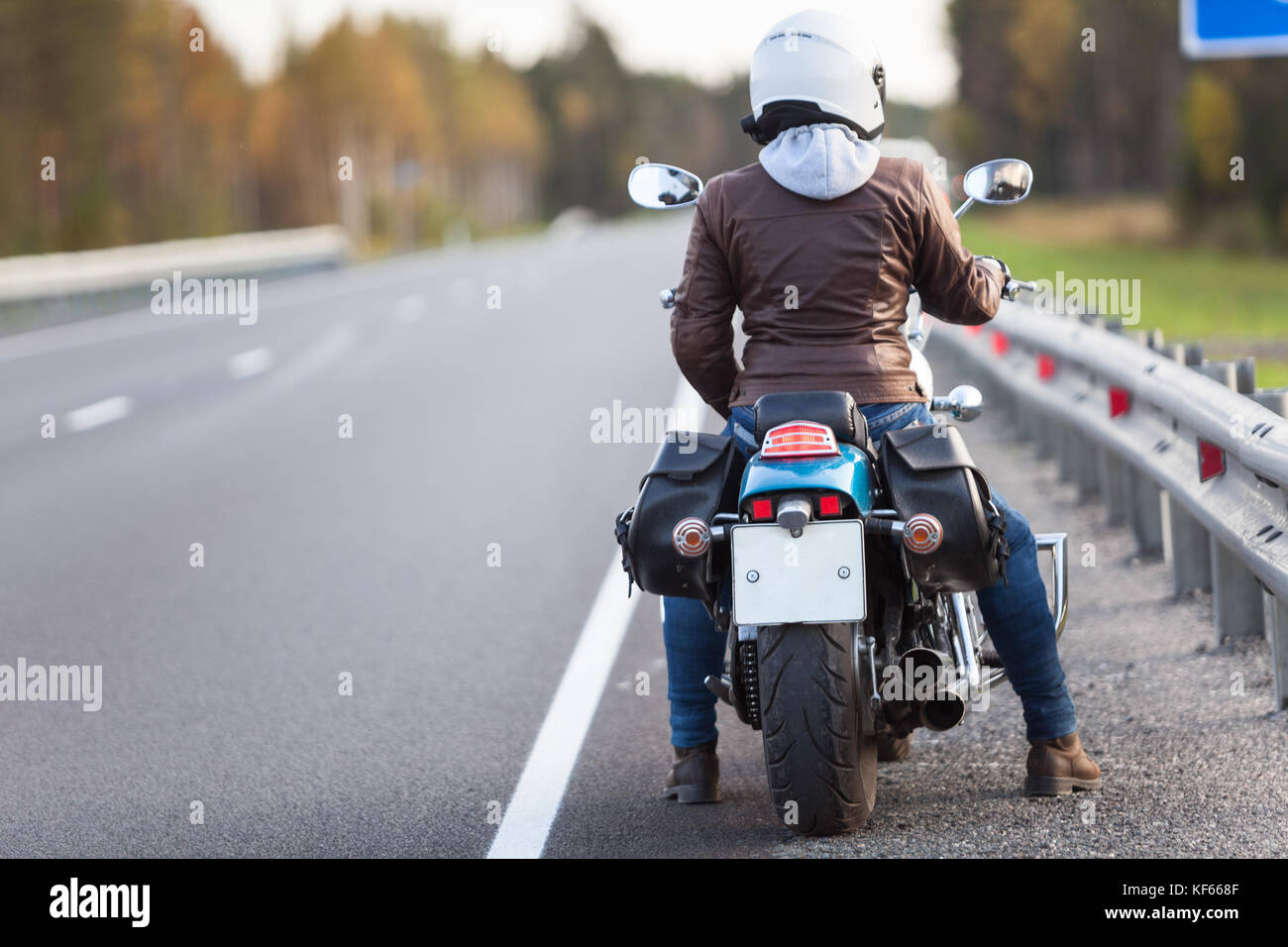 Rear view at woman on a motorcycle resting on the roadside of a country ...