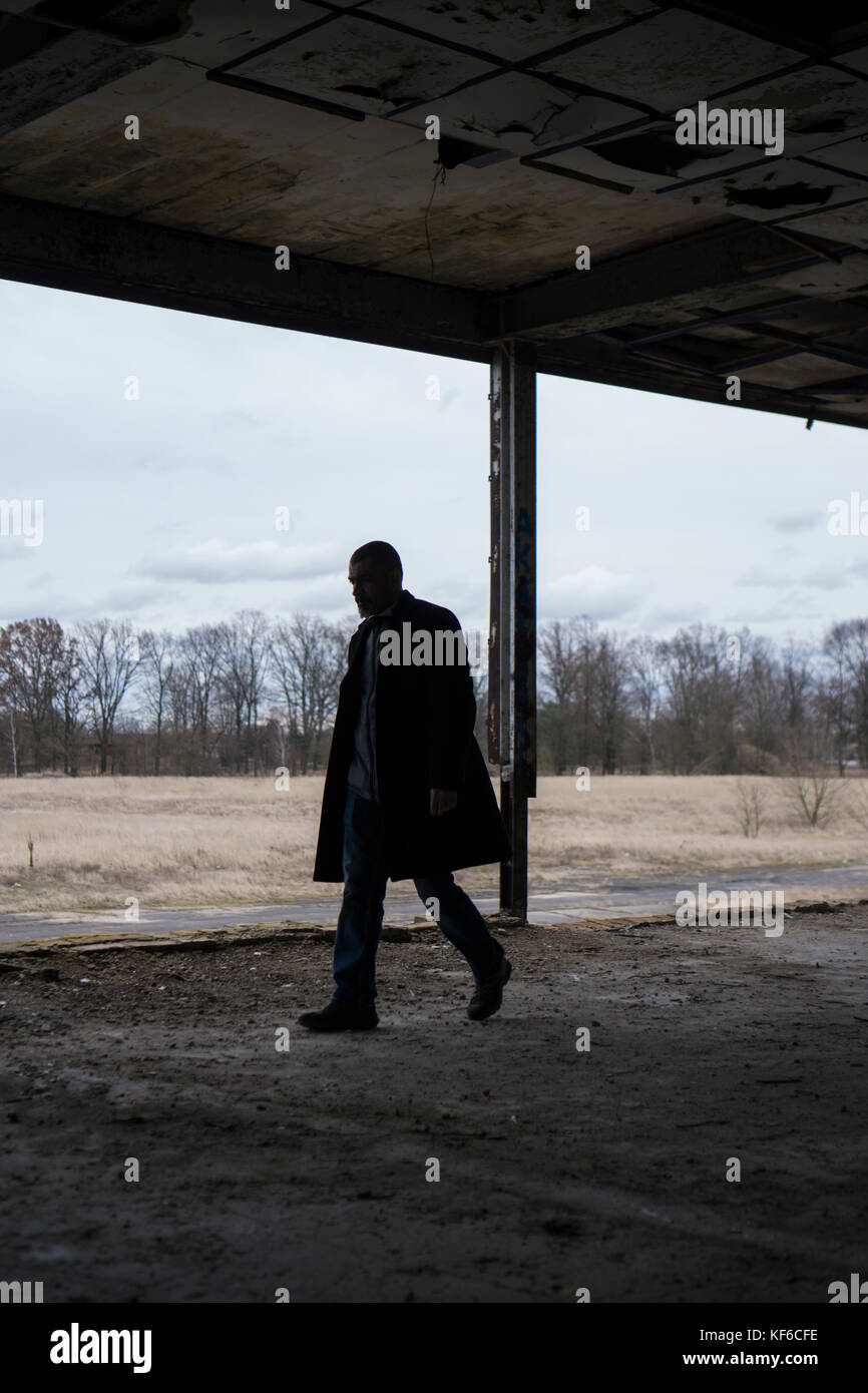Side view of a man wearing a coat walking inside a derelict building ...