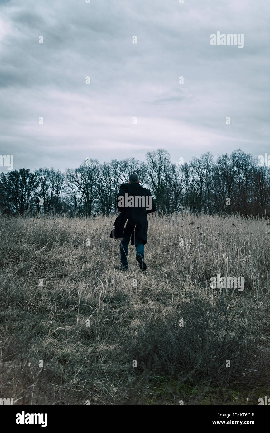 Rear view of a man running away in a field Stock Photo - Alamy
