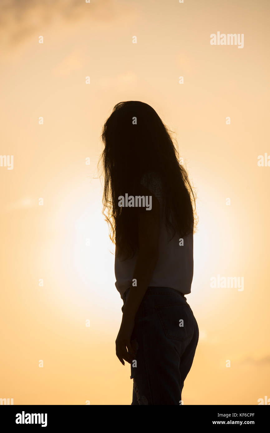 Silhouette of a young woman standing against a sunset sky Stock Photo ...