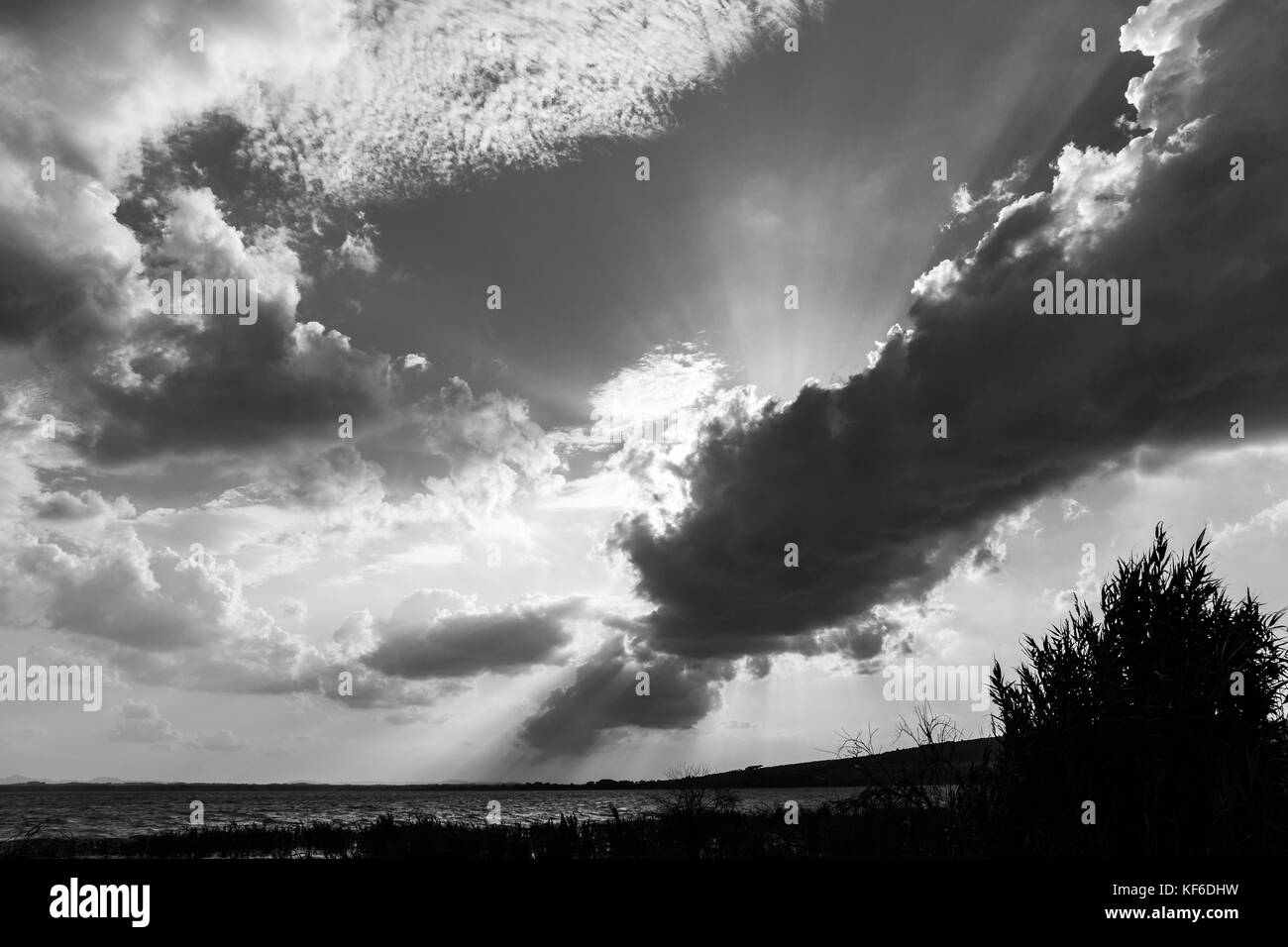Powerful sun rays coming out through some clouds above a lake shore ...