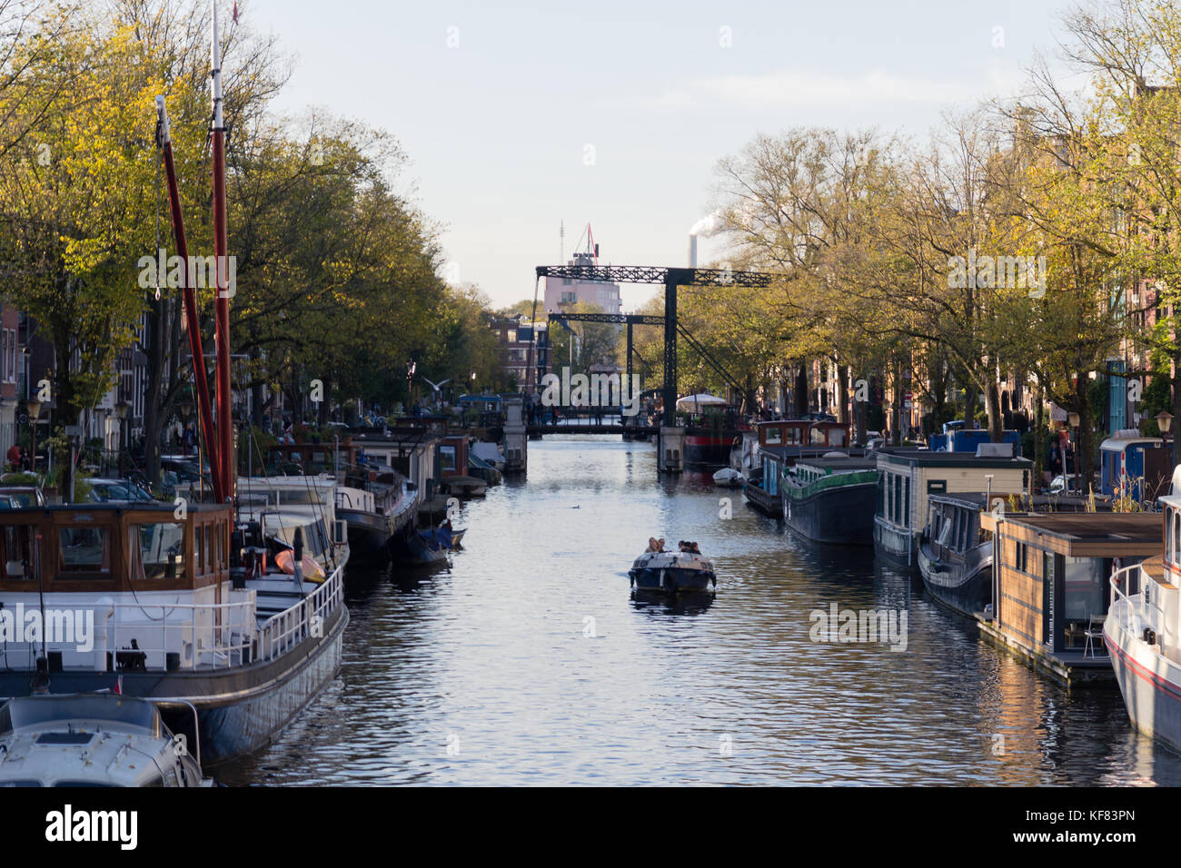 Boat sailing over Amsterdam canal with house boats on either side and ...