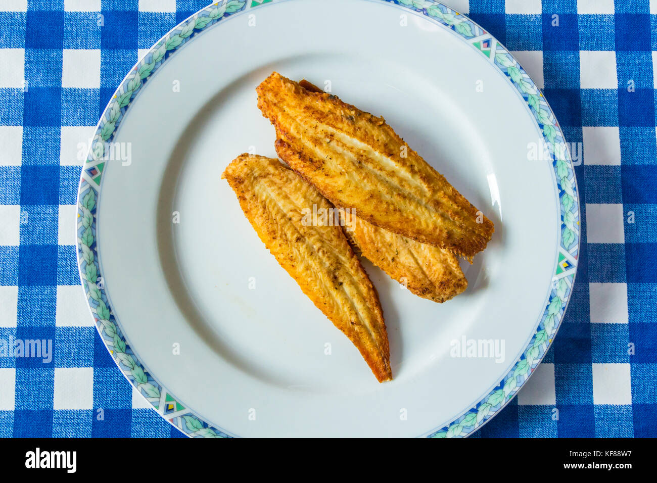three small fried dover sole fish on white plate with blue and white ...